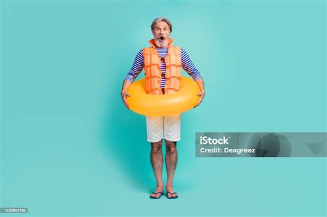 재미 미친 노인 수영 스탠드 내부 서클 구명 부이 착용 줄무늬 선원 셔츠 흰색 반바지 오렌지 구명 조끼 플립 플롭 고립 된 청록색 색상 배경의 전체 길이 사진 수병에 대한