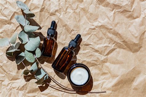 검은 고무 팁이있는 피펫이있는 호박색 유리 점적기 병과 건조한 유칼립투스가있는 종이 공예 배경에 크림 항아리를 엽니 다 자연 피부 개념 유기농 스파 화장품 트렌디 한 개념