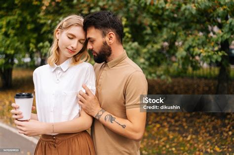 나무를 배경으로 도시 공원에서 눈을 감고 포옹하고 서 있는 사랑에 빠진 예쁜 젊은 부부의 전면 모습 수염 난 남자와 매력적인 여자 산책 20 24세에 대한 스톡 사진 및