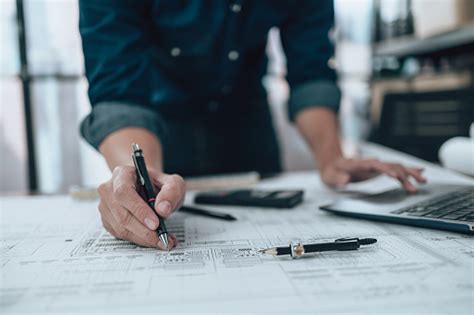 사무실 책상과 계산기 삼각형 눈금자 안전 안경 나침반 블루프린트의 버니어 캘리퍼에서 도면 검사 및 쓰기로 작업하는 엔지니어링 엔지니어 건축가 산업 및 공장 개념 개발에 대한