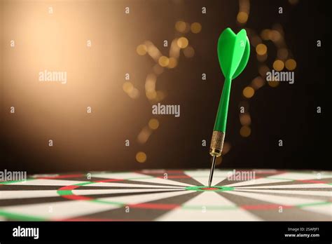 Green Arrow Hitting Target On Dart Board Against Black Background With Blurred Lights Closeup
