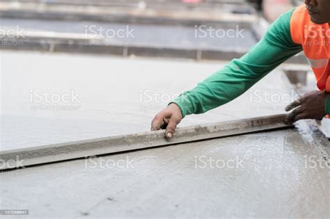 콘크리트 바닥을 매끄럽게 평평하게 하여 작업하는 건설 기술자 건설 노동자는 건설 현장에서 젖은 콘크리트를 붓는 긴 흙손을 사용합니다 콘크리트의 매끄러운 표면을 만드는 메이슨