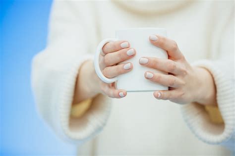 니트 흰 스웨터에 젊은 여자입니다 화이트 컵의 차 또는 차를 손에 들고 있습니다 파란색 벽의 배경에 고립 스튜디오의 초상화 사람들의 삶의 방법의 개념입니다 레이아웃 공간의