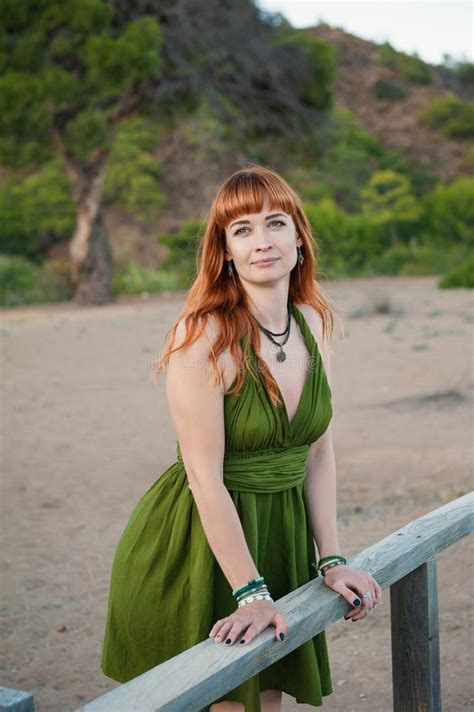 Charming Redhead Girl In A Green Dress Poses Against A Sandy Landscape