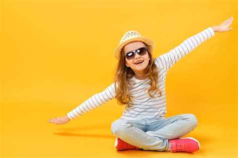 바닥에 앉아 비행 여행을 꿈꾸는 즐거운 어린 소녀 스튜디오에서 노란색 배경에 모자와 선글라스와 함께 행복 귀여운 아름다운 아이 전체 길이 개념에 대한 스톡 사진 및 기타