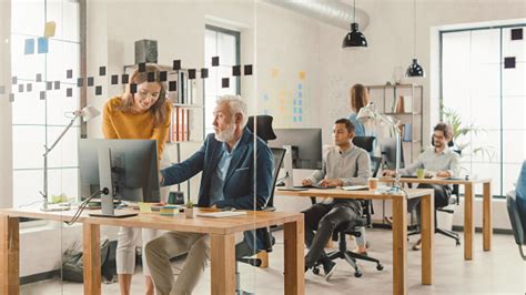 데스크톱 컴퓨터에서 작업 하는 책상에 앉아 잘 생긴 중년 창조적 인 엔지니어는 아름 다운 여성 프로젝트 관리자와 토론을 친절한