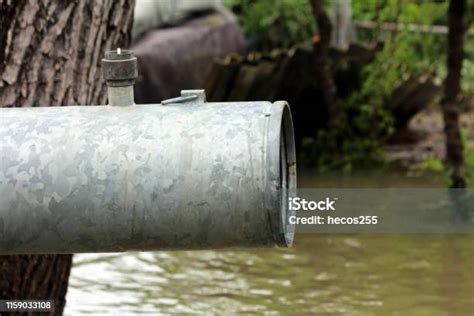 모래 상자 보호 벽을 통해 뒤뜰에서 홍수 물을 펌핑하는 데 사용되는 오래된 나무 옆에 상단에 누락 된 규제 밸브와 큰 직경 강한 금속 파이프 0명에 대한 스톡 사진 및 기타