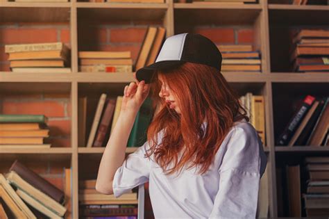 템플릿 빈 티셔츠와 건강한 주근깨 피부를 가진 모자를 입은 빨간 머리 여성의 초상화 책장 배경에 포즈를 취하는 젊은 백인 모델 공간을 복사하고 모의를 바하십시오 인시브를