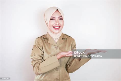 갈색 유니폼과 히잡을 쓴 젊은 아시아 무슬림 여성이 스튜디오 흰색 고립된 배경의 빈 공간을 가리키고 있다 25 29세에 대한 스톡 사진 및 기타 이미지 Istock