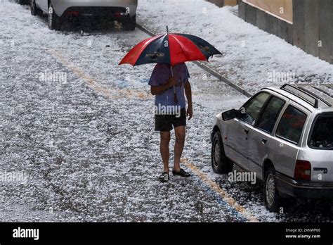 A Person Holding An Umbrella Checks The Damage To A Car After A Hail
