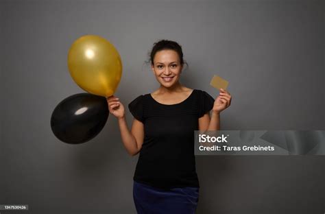 금 신용 카드 또는 할인 카드를 들고 미소 짓는 아프리카 여성의 초상화와 팽창 된 검은 색과 금색 공기 풍선과 복사 광고 공간으로 회색 벽 배경에 포즈를 취하는 카메라를