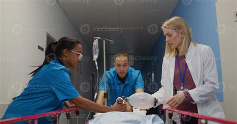 Medical Workers Carry A Patient On A Gurney Along The Hospital Corridor