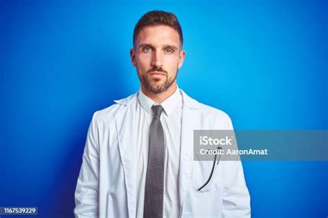 젊은 잘 생긴 의사 남자 얼굴에 심각한 표정으로 고립 된 배경 위에 흰색 전문 코트를 입고 카메라를 보는 간단하고 자연스러운 의사에 대한 스톡 사진 및 기타 이미지 Istock