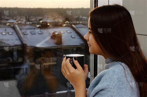 一个不错的女孩喝着咖啡看着窗外的夕阳