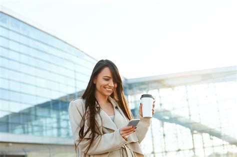 비즈니스 여성이 커피 한 잔을 들고 사무실 근처에서 전화를 사용하고 있습니다 아름 다운 미소 짓는 여성의 초상화 휴대 전화를 들고 야외에 서있다 전화 통신 25 29세에
