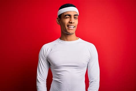 젊은 잘 생긴 아프리카 계 미국인 스포츠맨 은 섹시한 표정 쾌활하고 행복한 얼굴로 카메라를보고 윙크 빨간 배경 윙크 위에 스포츠웨어를 입고 관능에 대한 스톡 사진 및 기타