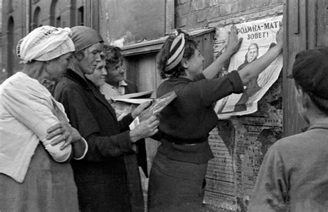 Женщина наклеивает на доску объявлений плакат «Родина мать зовёт — военное фото