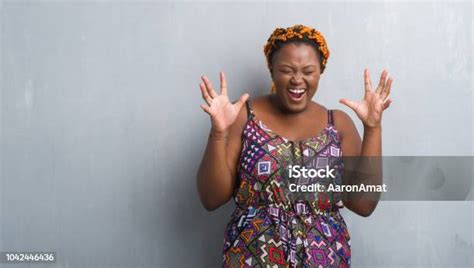 오렌지 입고 회색 그런 지 벽에 젊은 아프리카계 미국인 여자는 미친 축 하 머리 띠 무기와 성공을 위해 미친 제기 하 고 흥분 비명 눈을 폐쇄 우승자 개념 땋은 머리에 대한