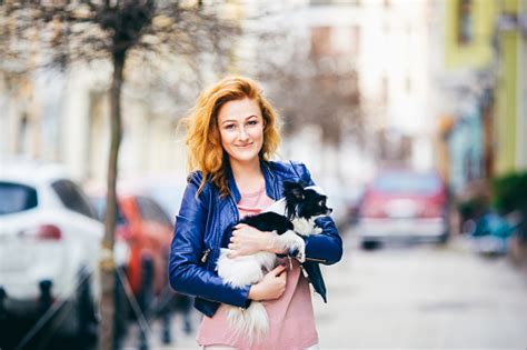 제목 남자 고 개입니다 얼굴에 주 근 깨와 빨간 머리 젊은 백인 여자 흑인과 백인 얽히고 설킨 치와와 품종 개를 보유 하고있다 블루 가죽 자 켓 입은 여자 봄 바쁜 거리에