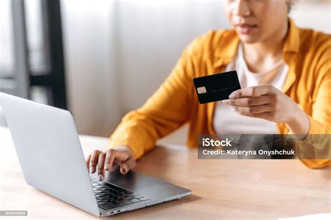 온라인 쇼핑 및 결제 캐주얼 한 옷을 입고 테이블에 앉아 온라인 구매 비용을 지불하고 그녀의 손에 카드를 들고 노트북에 신용 카드 정보를 입력 25 29세에 대한 스톡 사진