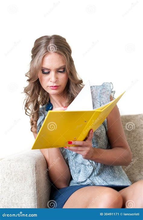 Женщина читая книгу и усмехаясь по мере того как она сидит на стуле Стоковое Изображение