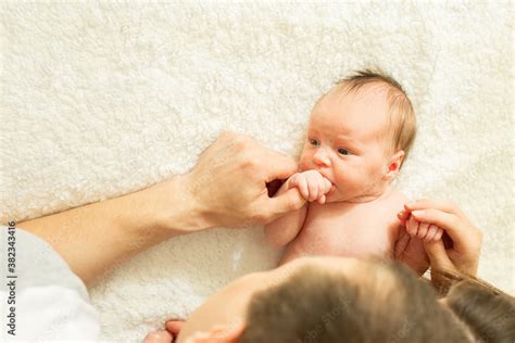 Cute Naked Newborn Baby With Open Eyes Lying On A Bed A Parent Holds The Legs Of A Newborn