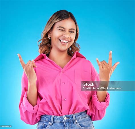 윙크 초상화 그리고 푸른 배경에 자유 행복하고 긍정적인 태도를 위해 스튜디오에서 로커 손을 가진 여자 록스타 이모티콘 사인 또는 펑크 제스처 좋은 기분 또는 분위기가 있는