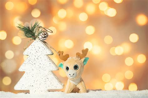 흰색 장난감 전나무와 봉제 장난감 사슴이 보케 조명을 배경으로 눈 속에 있습니다 공간을 복사합니다 새해 복 많이 받으세요 그리고 아이를 위한 메리 크리스마스 인사말 카드 0