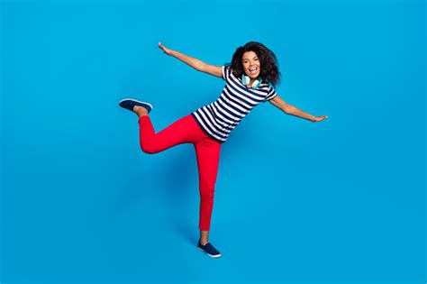 긍정적 인 펑키 재미 Afro 미국 소녀의 전체 길이 사진은 음악 홀드 손을 듣고 휴식 헤드셋을 가지고 그녀가 새 착용 스트라이프 티셔츠 캐주얼 의상 고립 된 파란색 색상