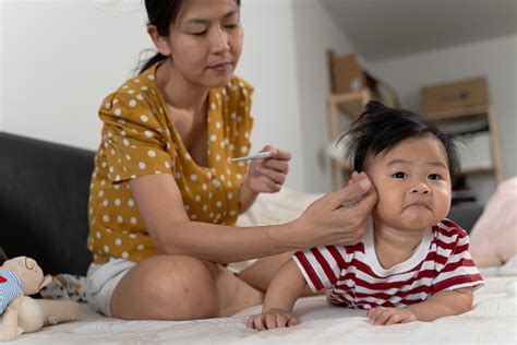 젊은 아시아 어머니는 인플루엔자 열병으로 인한 질병 중에 아기 아들의 체온을 확인하기 위해 디지털 온도계와 손을 돌보고