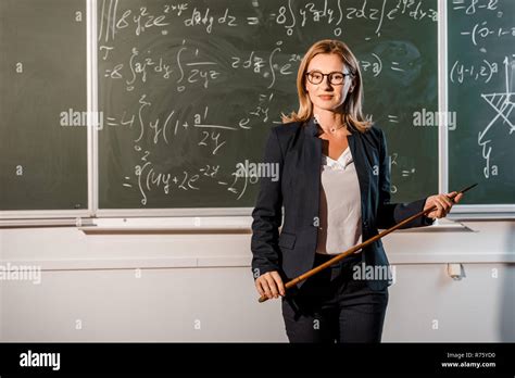 Attractive Female Teacher With Wooden Pointer Explaining Mathematical Equations In Classroom