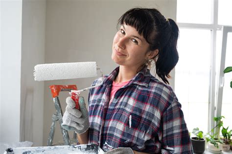 페인트 롤러를 입은 행복한 여자와 손에 벽을 위한 흰색 페인트 클로즈업 초상화 집안의 건축 작업 및 미용 수리 벽화 착색 자신의 손으로 마무리 작업 30 34세에 대한 스톡