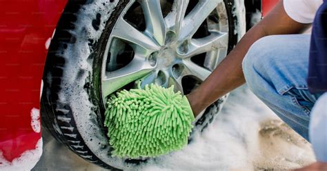 녹색 스폰지를 들고 거품으로 자동차 바퀴를 씻는 아프리카 남자의 손 야외 셀프 세차 서비스에서 고급 빨간 자동차의 현대적인 림