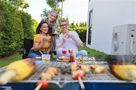 다양한 연령대의 행복한 가족이나 친구들이 바비큐를 만들고 레드 와인 한 잔과 함께 야외에서 축하하고 옥수수를 굽고 여름날 집 뒤뜰 정원에서 바베큐 파티를 즐긴다 가정 생활에