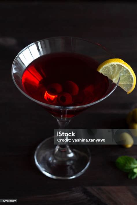바에서 국제적인 칵테일을 즐기며 즐기신다 올리브와 레몬을 곁들인 붉은 칵테일 마티니 유리와 녹색 민트를 나무 배경에 얹습니다 검은 테이블에 마티니 안경 복사 공간을