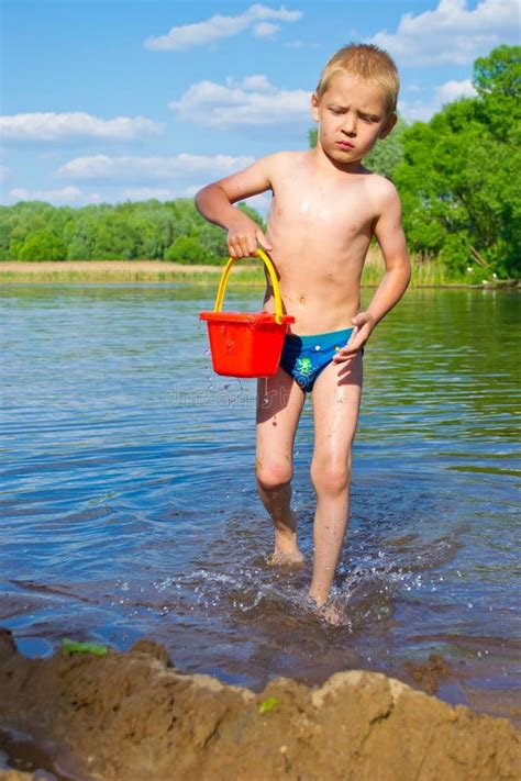 Мальчик играет с песком на пляже плавая на озере Стоковое Изображение изображение