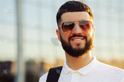 在阳光明媚的日子里一个戴着墨镜穿着休闲白衬衫的男人微笑着一个在室外玻璃建筑附近的人