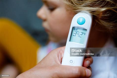 어머니는 집에서 귀 온도계에 적외선을 가진 그녀의 작은 유치원 딸 아픈 아이를 위해 온도를 취합니다 디지털 적외선 온도계를 들고 있는 고학년 발열 어머니 손 아이에 대한