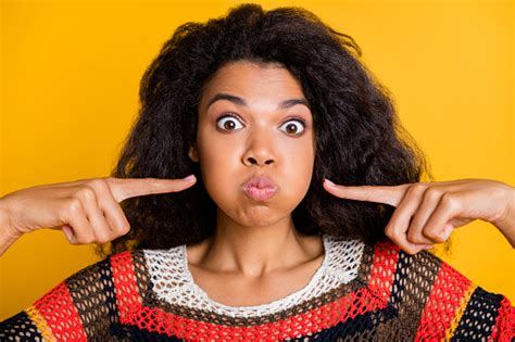 그녀의 뺨 포인트 검지 손가락을 팽창 재미 펑키 십대 어두운 피부 소녀의 사진을 닫는 것은 노란색 색상 배경을 통해 고립 된 세련된 줄무늬 스웨터를 착용 농담을 원한다