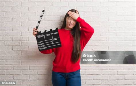 머리에 손으로 압박 하는 판자를 들고 흰 벽돌 벽을 통해 젊은 중국 여자는 수치심과 깜짝 얼굴로 충격 분노와 좌절 두려워 하 고 실수에 대 한 화가 감독에 대한 스톡 사진