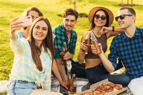 캐주얼 한 옷을 입고 음식과 차가운 음료를 즐기고 풀밭에 앉아있는 야외 에서 웃고있는 젊은 사람들의 그룹 먹기에 대한 스톡 사진 및 기타 이미지 Istock