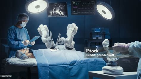 Ar 헤드셋을 착용한 외과 의사는 고정밀 원격 제어 로봇 팔을 사용하여 환자를 수술하고 동료는 병원에서 태블릿으로 바이탈을 확인합니다 로봇 팔다리로 일하는 의사 수술에 대한