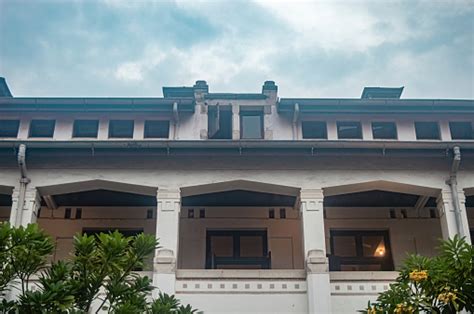 흐린 하늘을 배경으로 아치형 창문과 무성한 녹지가 있는 유서 깊은 건물 외관입니다 이 건축물은 향수를 불러일으키는 분위기를 연출하는 고전적인 디자인 요소를 갖추고 있습니다