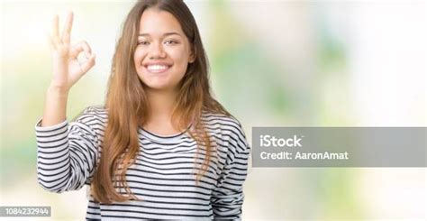 젊은 아름 다운 갈색 머리 여자 격리 된 배경 손과 손가락으로 Ok 사인을 하 고 긍정적인 미소에 줄무늬 스웨터를 입고 성공적인 식입니다 긍정적인 감정 표현에 대한 스톡