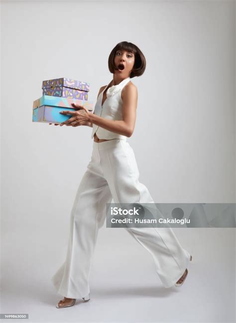 뭉툭한 머리를 한 세련된 흰색 의상을 입은 웃는 여자가 선물 상자를 손에 들고 흰색 배경을 걷고 있다 여자에 대한 스톡 사진 및 기타 이미지 Istock