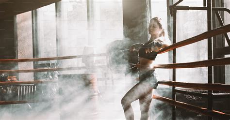 반지에 서 있는 젊은 예쁜 권투 선수 여자 검은색 스포츠 브래지어 회색 바지 링에 서서 밧줄에 기대어 있는 트레이너를 입은