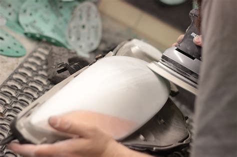 연삭기를 사용한 헤드 라이트 유리 복원 한 남자가 주유소에서 연마기로 자동차 헤드라이트의 광학 장치를 연마합니다 연마 기계로