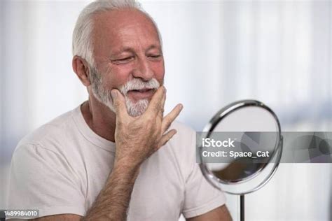 백발의 노인이 거울에 비친 자신의 모습을 바라보며 수염을 고치고 있다 미소 짓는 성숙한 남자는 외모에 만족합니다 노화와 아름다움 개념 노인 남자에 대한 스톡 사진 및 기타