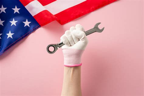 여성 노동력의 평등 작업용 장갑을 낀 여성의 손의 1인칭 평면도 파스텔 핑크 배경에 미국 국기 위에 렌치를 쥐고 있다 9월에