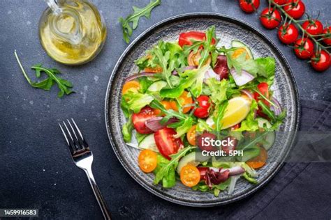 다채로운 체리 토마토 오이 적양파 양상추 라디치오 아루굴라를 곁들인 신선한 봄 비건 야채 샐러드 어두운 테이블 배경 상위 뷰
